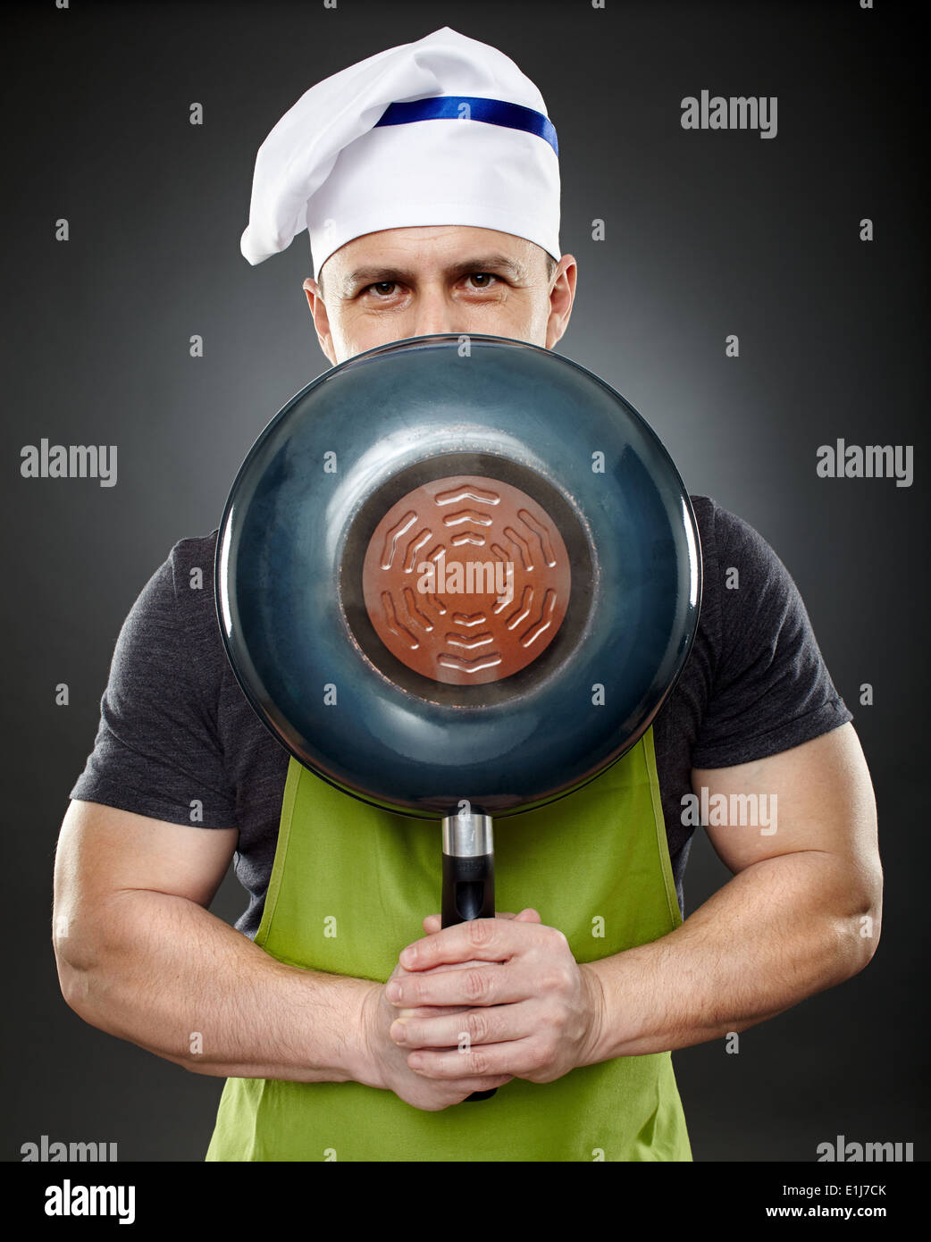 Studio shot of a man chef hiding his face behind a wok pan over gray ...