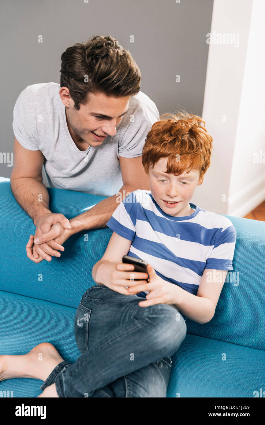 Father looking over shoulder of his son who is using a smart phone at ...
