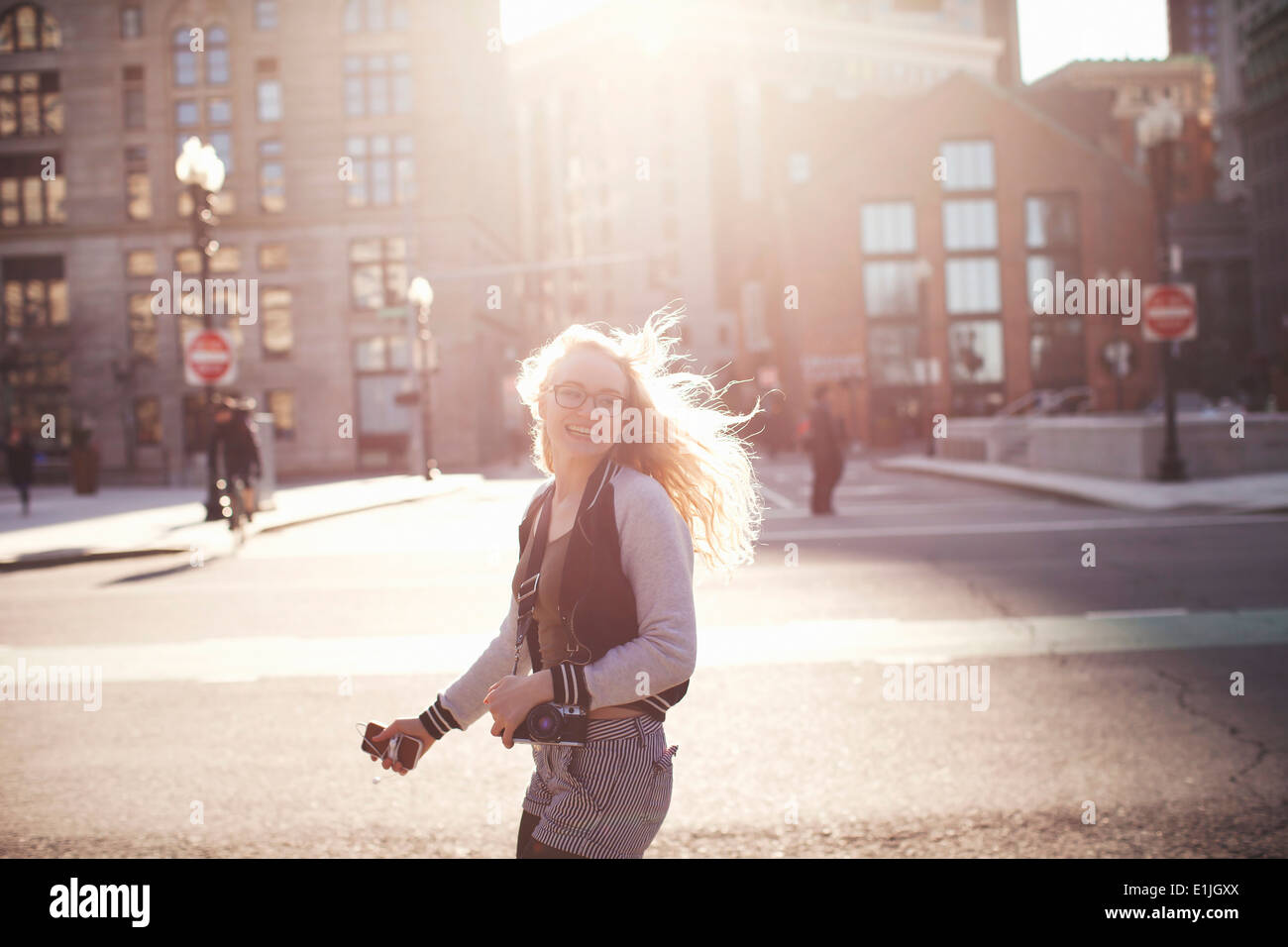 Young woman walking down street in Boston, carrying camera and ...
