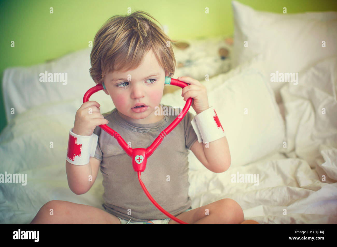Male toddler listening to toy stethoscope on bed Stock Photo - Alamy