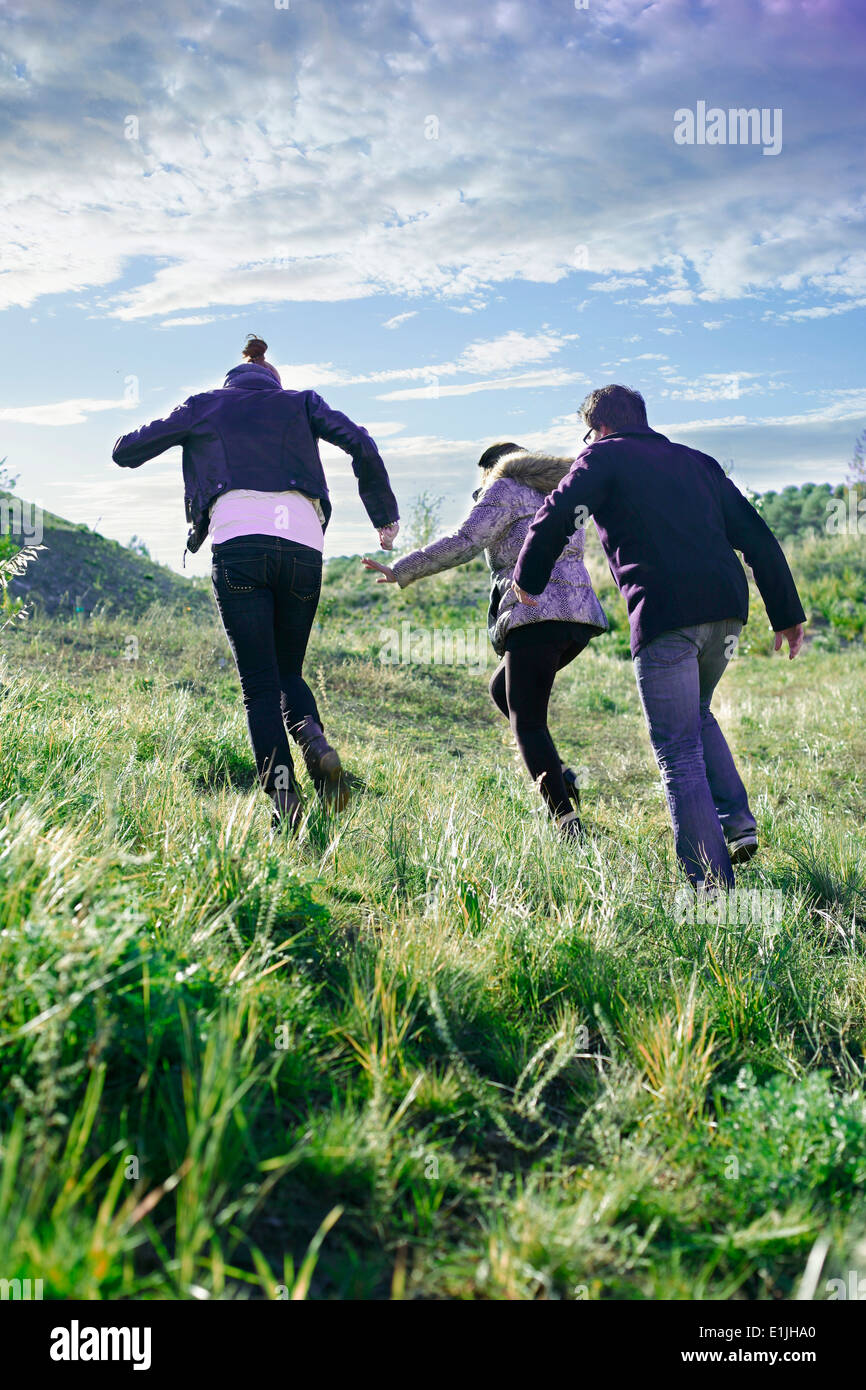 Three young adult friends running up grassy hill Stock Photo - Alamy