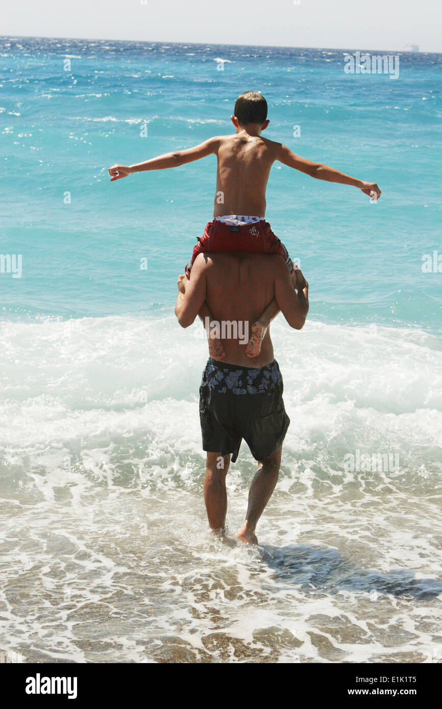 Young boy riding on big brothers shoulder in waves, West beach, Rhodes ...