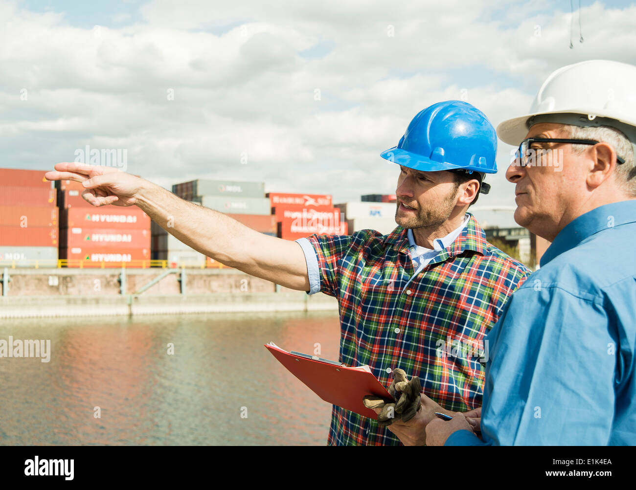 Two men with safety helmets talking at container port Stock Photo - Alamy