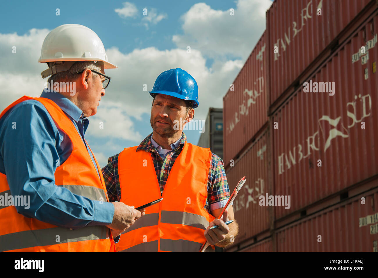 Two men with safety helmets and reflective vests talking at container ...