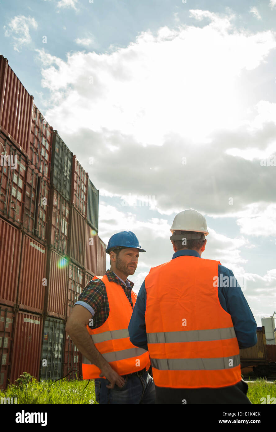Two men with safety helmets and reflective vests talking at container ...