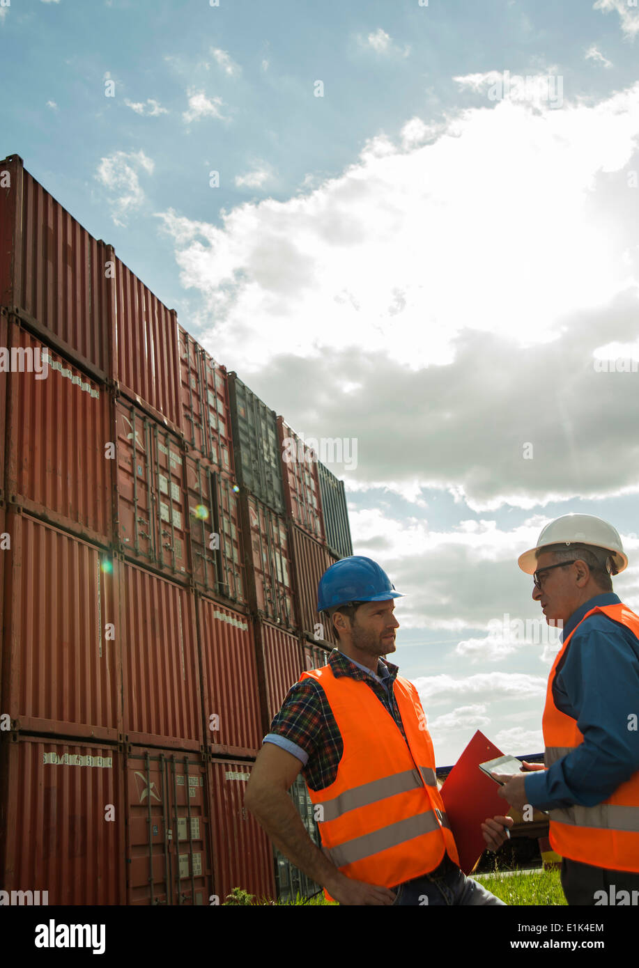 Two men with safety helmets and reflective vests talking at container ...