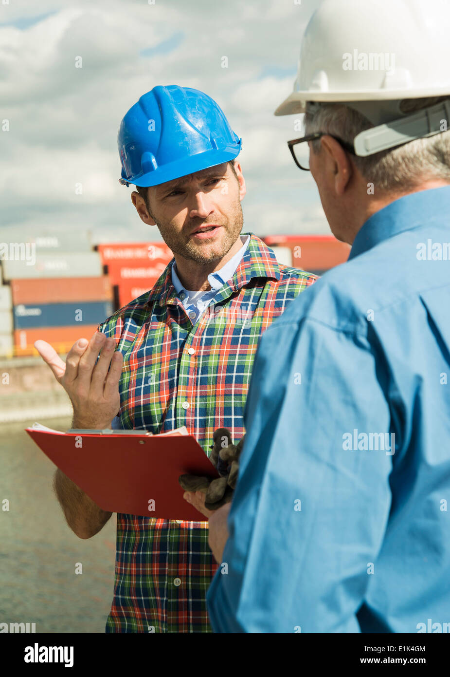 Two men with safety helmets talking at container port Stock Photo - Alamy