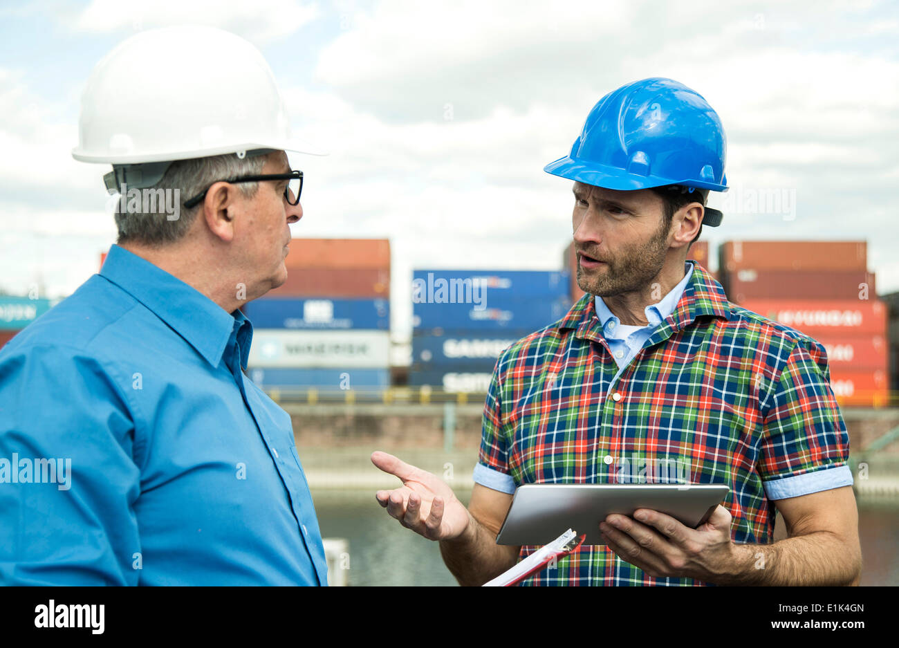 Two men with safety helmets talking at container port Stock Photo - Alamy