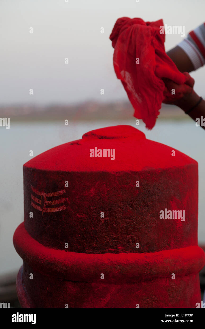 Spreading red powder on a lingam for Holi festival. The lingam is a ...