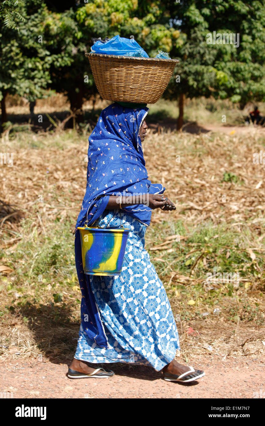 Woman walking and carrying a basket on her head Stock Photo - Alamy