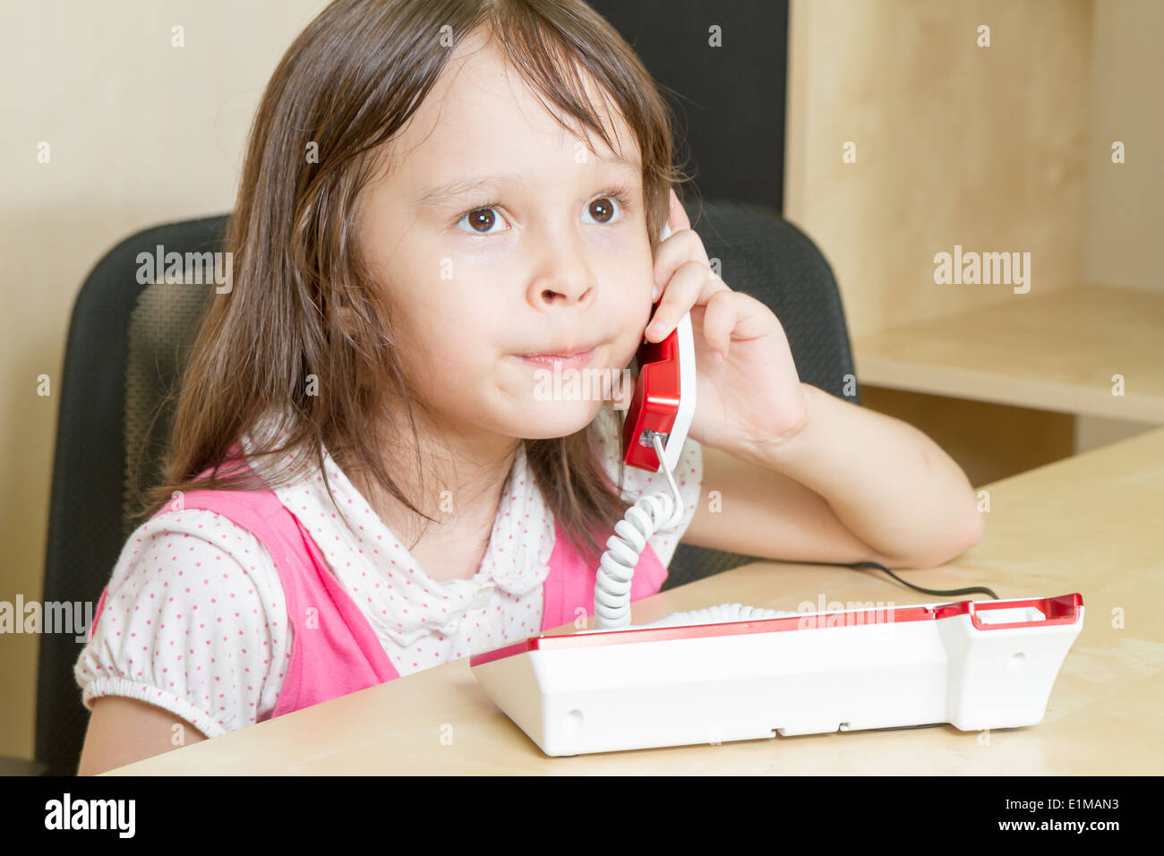 Little girl talking on red telephone at desk Stock Photo - Alamy
