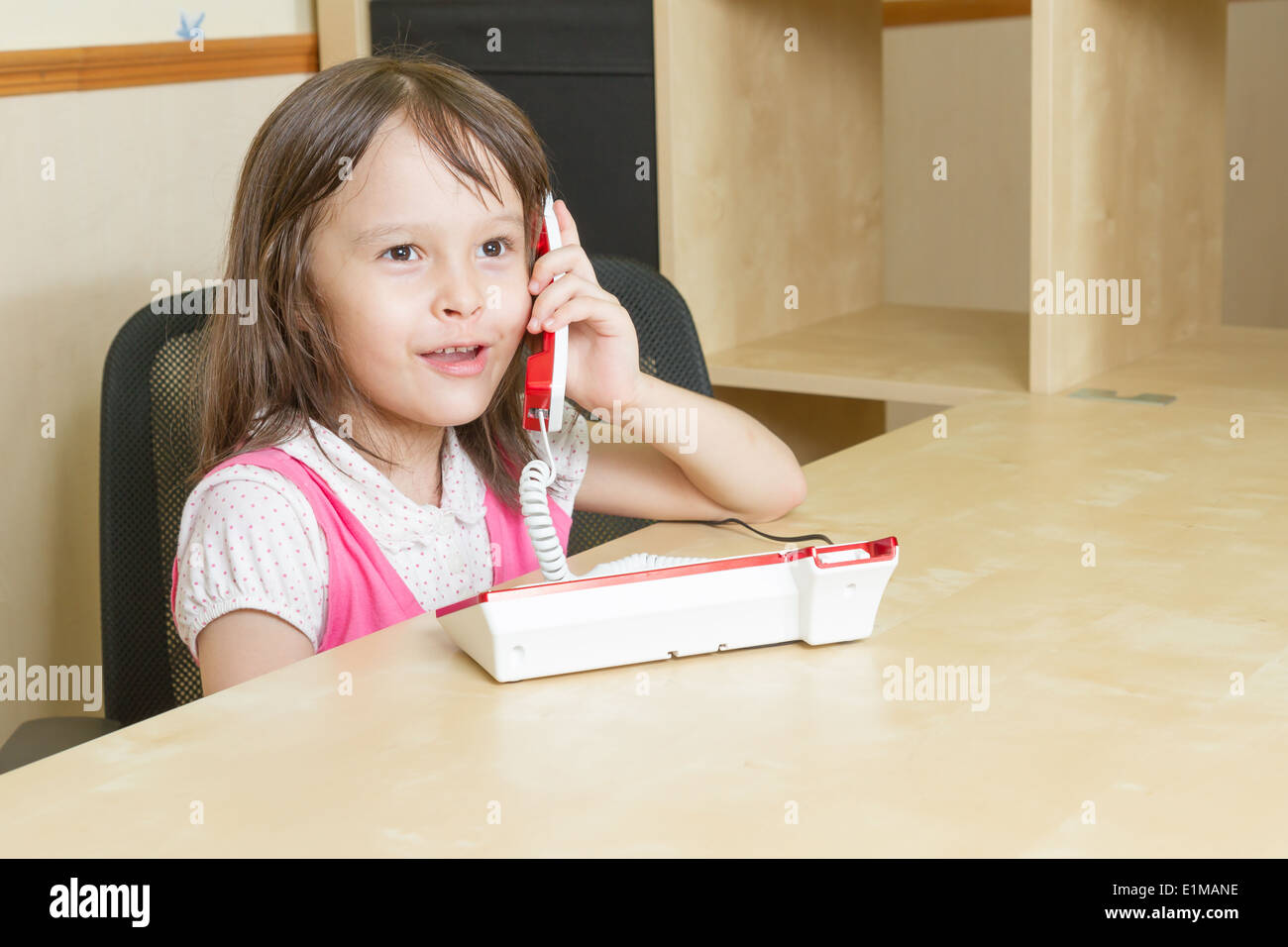 Little girl talking on red telephone at desk Stock Photo - Alamy