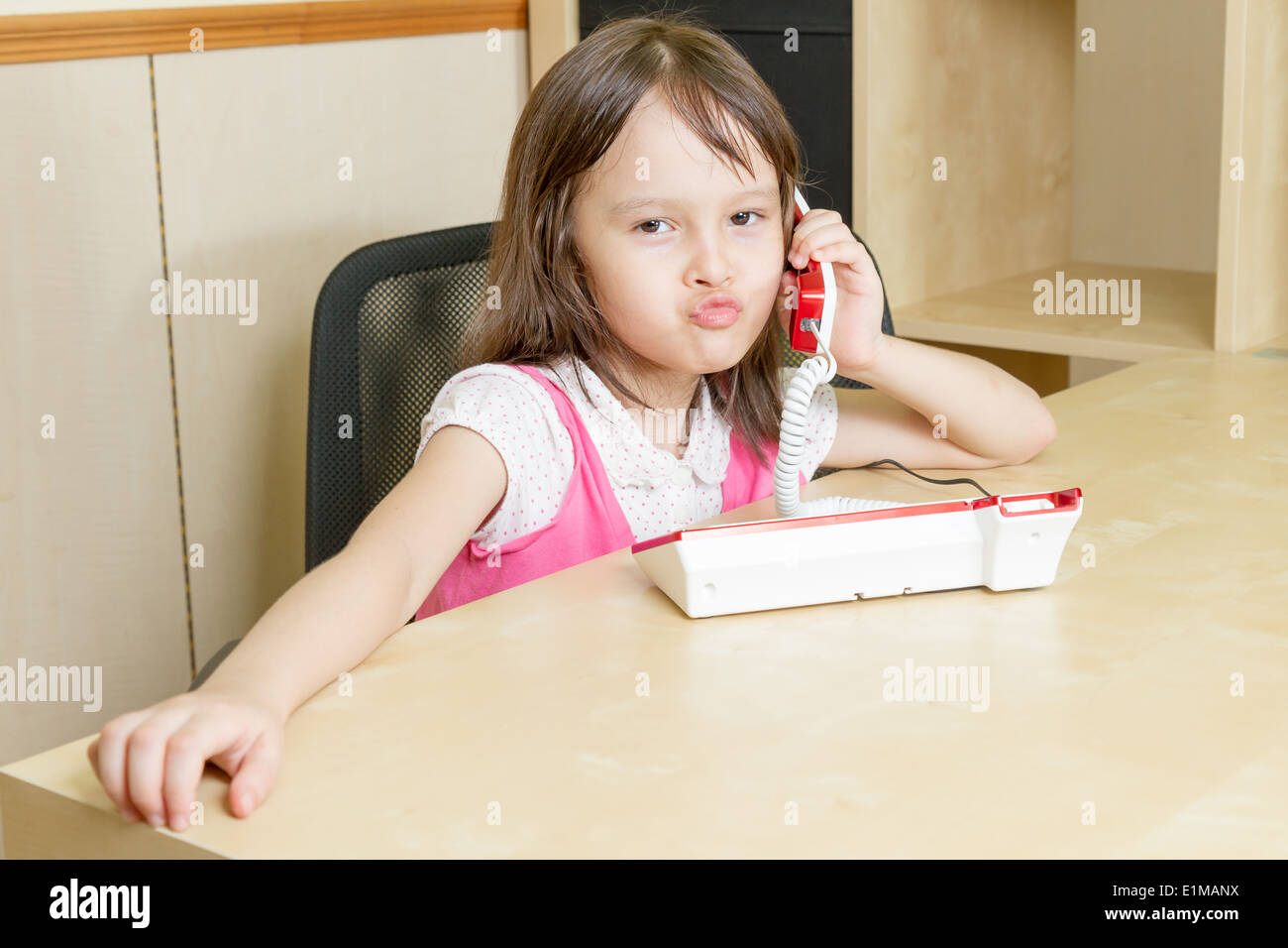 Little girl talking on red telephone at desk Stock Photo - Alamy