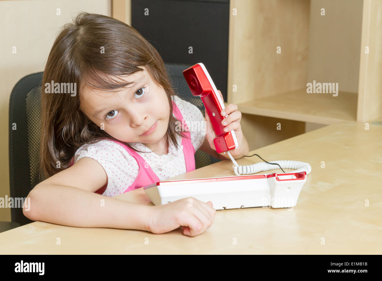 Little girl talking on red telephone at desk Stock Photo - Alamy