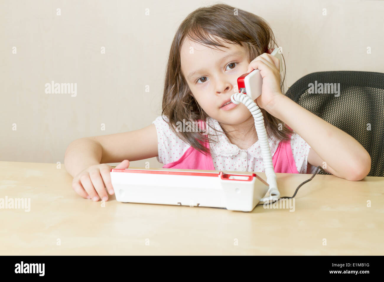 Little girl talking on red telephone at desk Stock Photo - Alamy