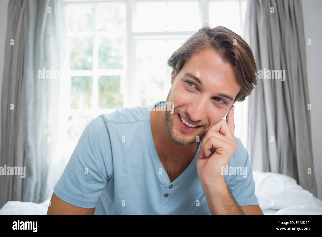 Handsome smiling man sitting on bed Stock Photo - Alamy