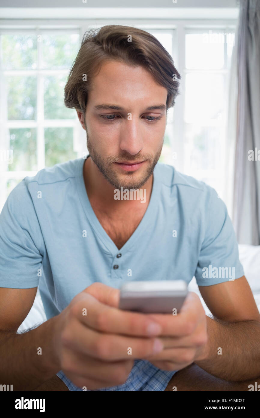 Handsome man sitting on bed sending a text message Stock Photo - Alamy