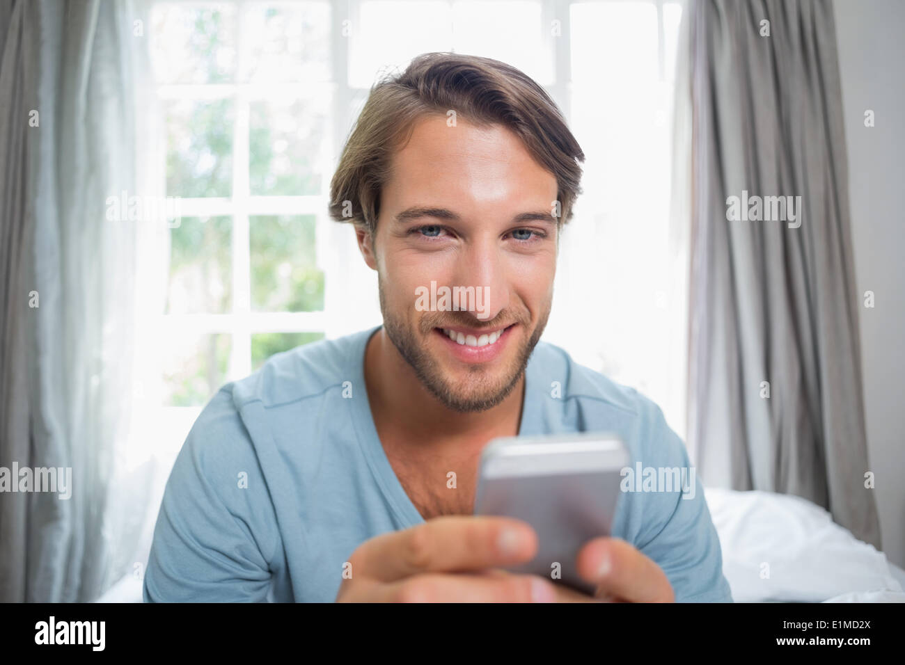 Handsome man sitting on bed sending a text message Stock Photo - Alamy