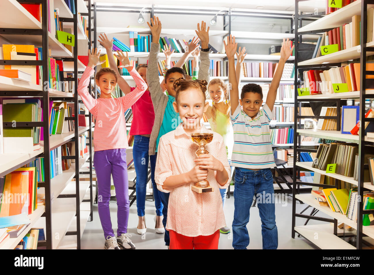 Smiling girl holds golden cup, kids jump behind Stock Photo - Alamy