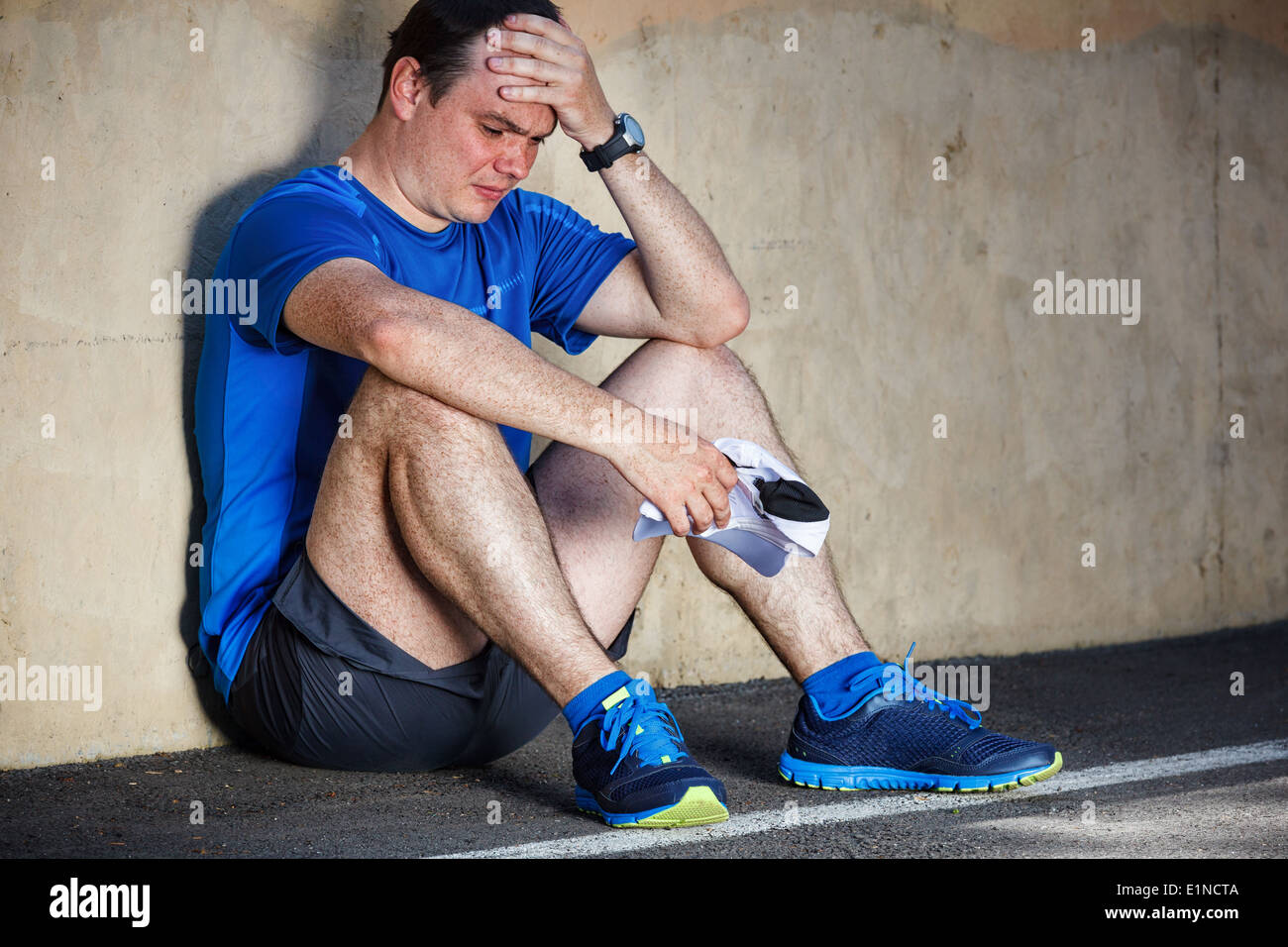 Upset Young male runner resting leaning against wall Stock Photo - Alamy