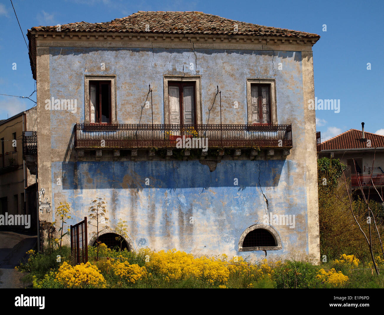Faded facade of blue washed abandoned building with rusty iron balcony ...