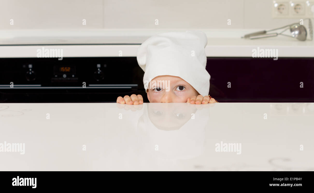 Child in a chefs toque hiding behind a counter in the kitchen so that ...