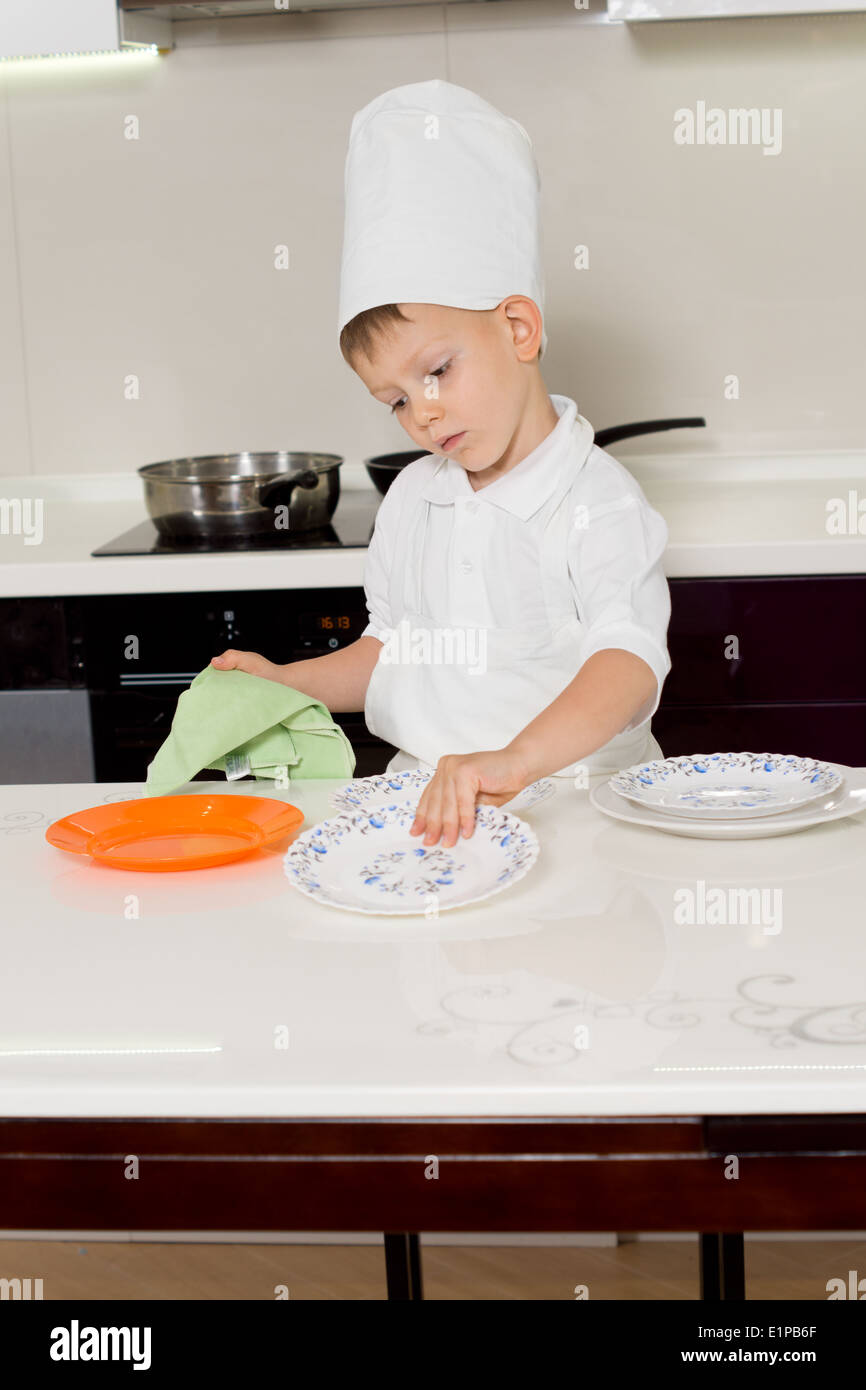 Cute little boy chef getting ready for dinner wiping and cleaning the ...