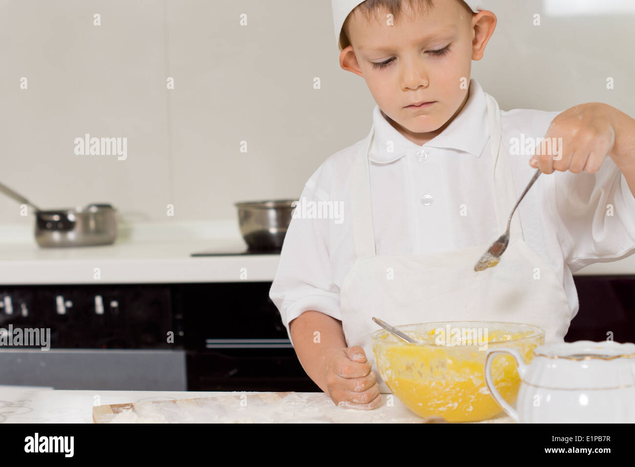 Little boy in a chefs toque and apron standing at the kitchen counter ...