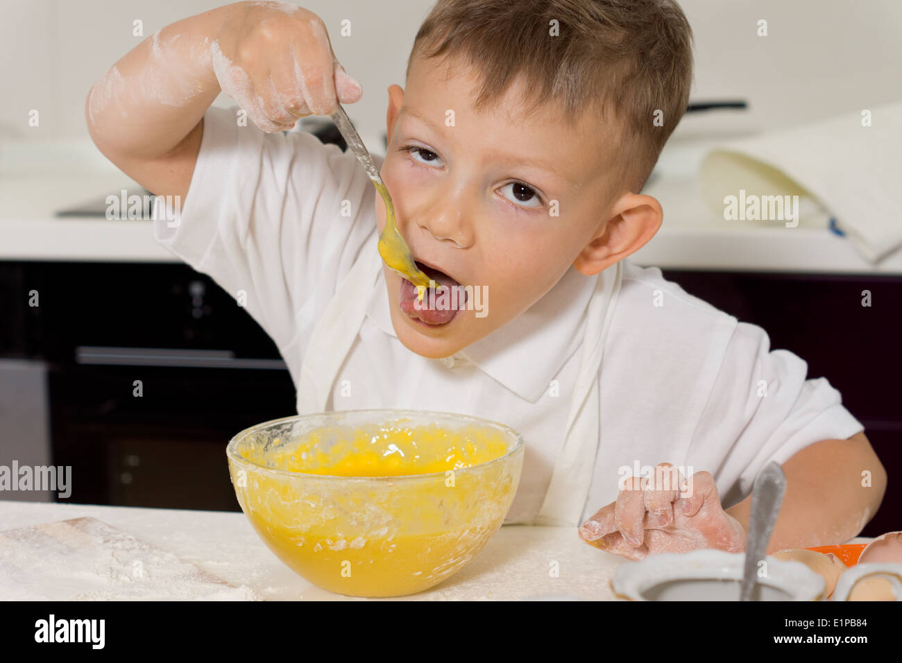 Young boy taking a taste of the cake mix as he stands in the kitchen ...