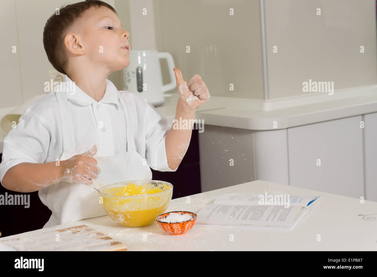 Little boy baking in the kitchen giving a thumbs up of approval as he ...