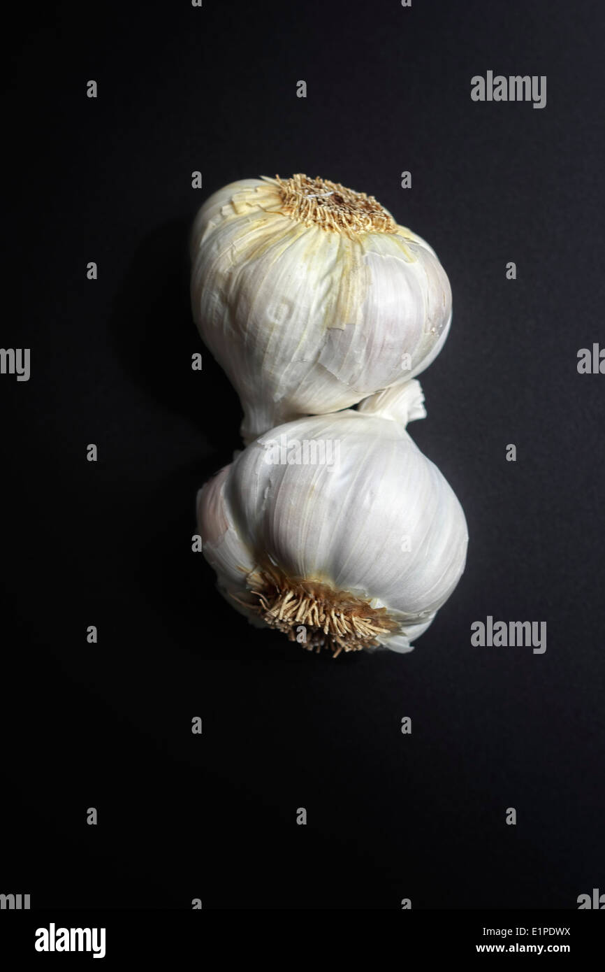 Two bulbs of garlic lay nestled up together on top of a black table top ...