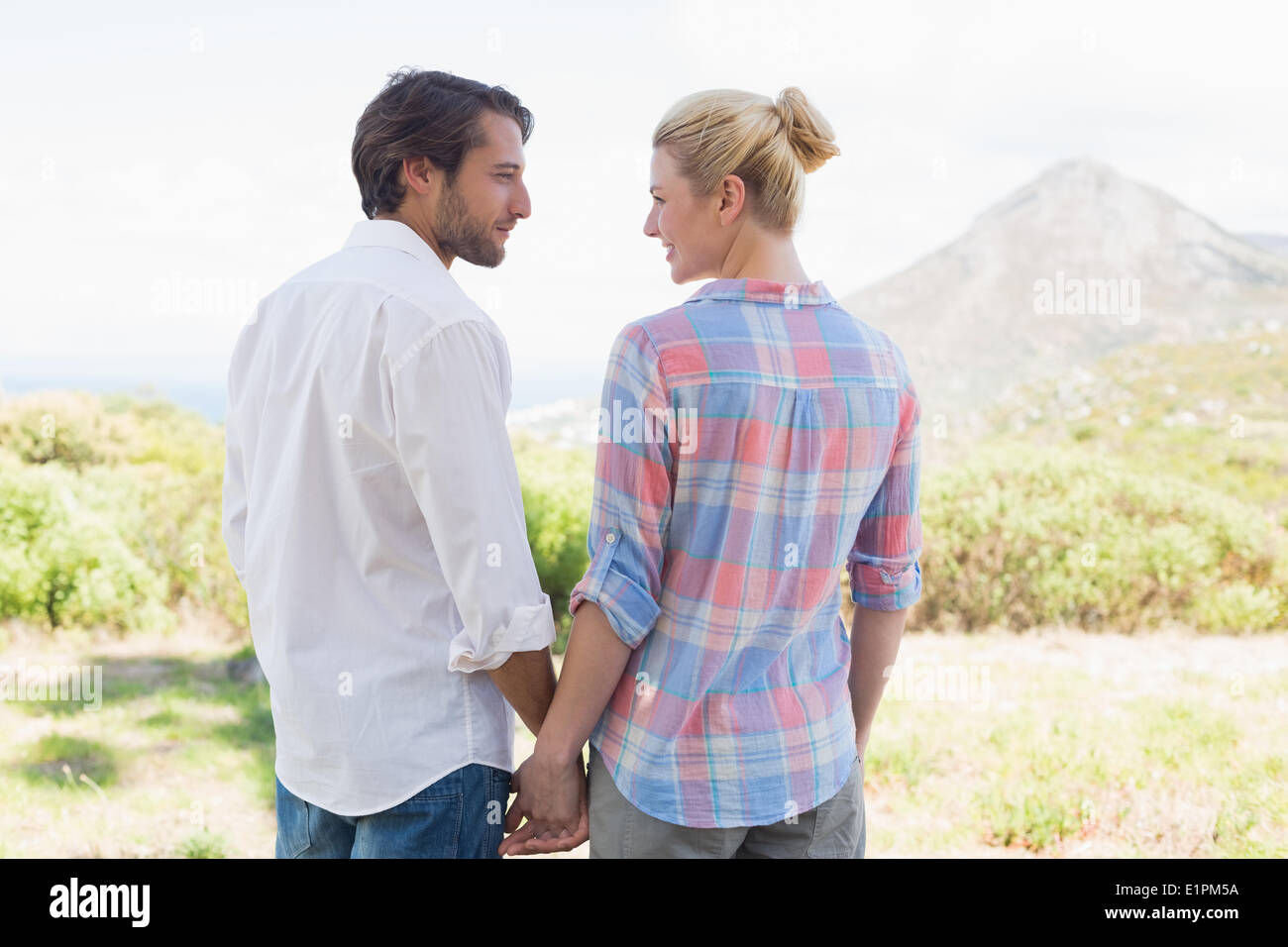 Cute couple standing hand in hand smiling at each other Stock Photo - Alamy