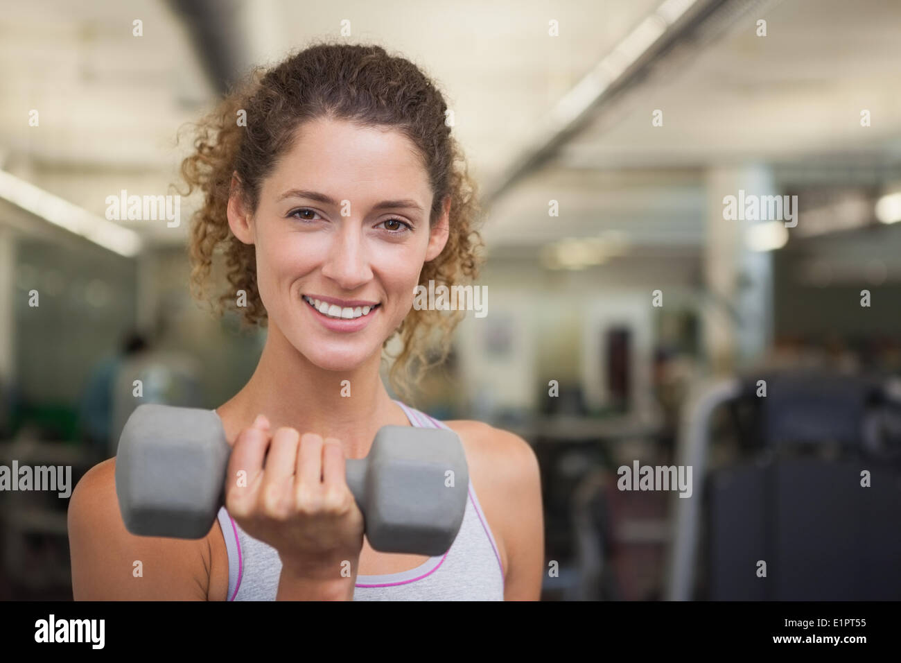 Fit woman smiling at camera lifting dumbbell Stock Photo - Alamy