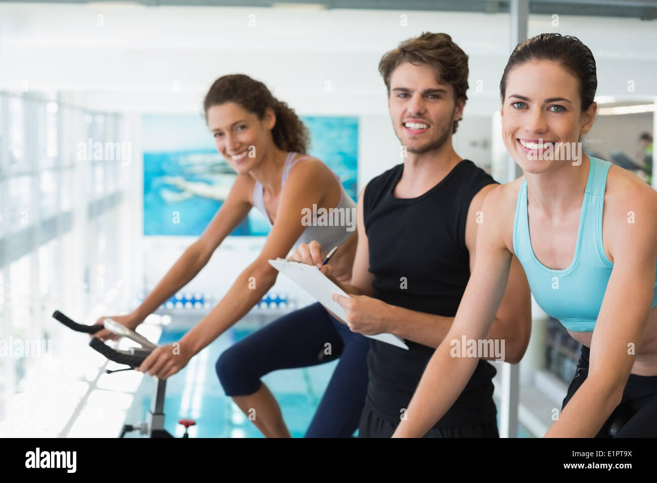 Fit women in a spin class with trainer taking notes and smiling at ...
