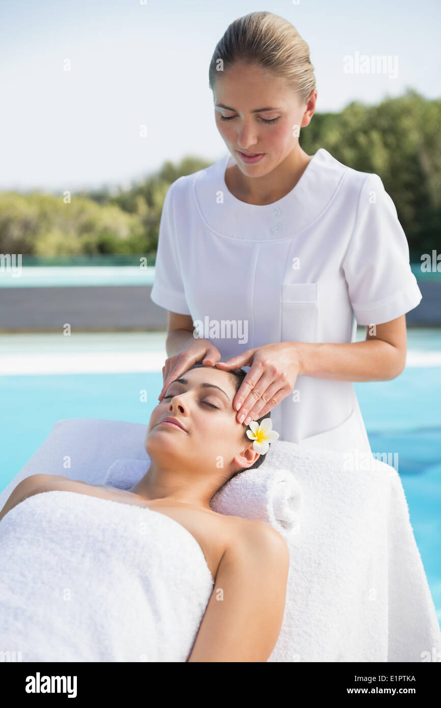 Tranquil brunette getting a head massage poolside Stock Photo - Alamy