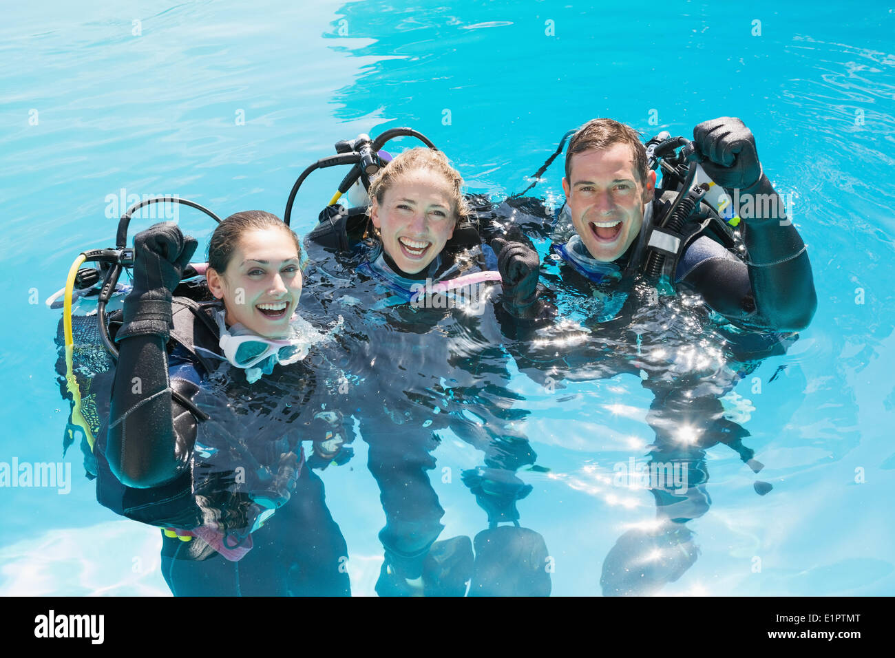 Smiling friends on scuba training in swimming pool cheering at camera ...