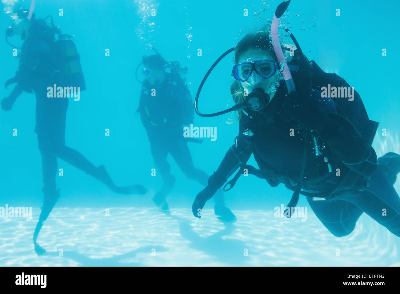 Friends on scuba training submerged in swimming pool one looking to ...