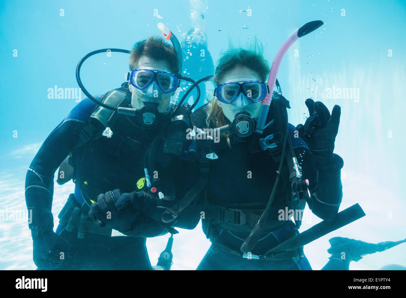 Friends on scuba training submerged in swimming pool looking to camera ...