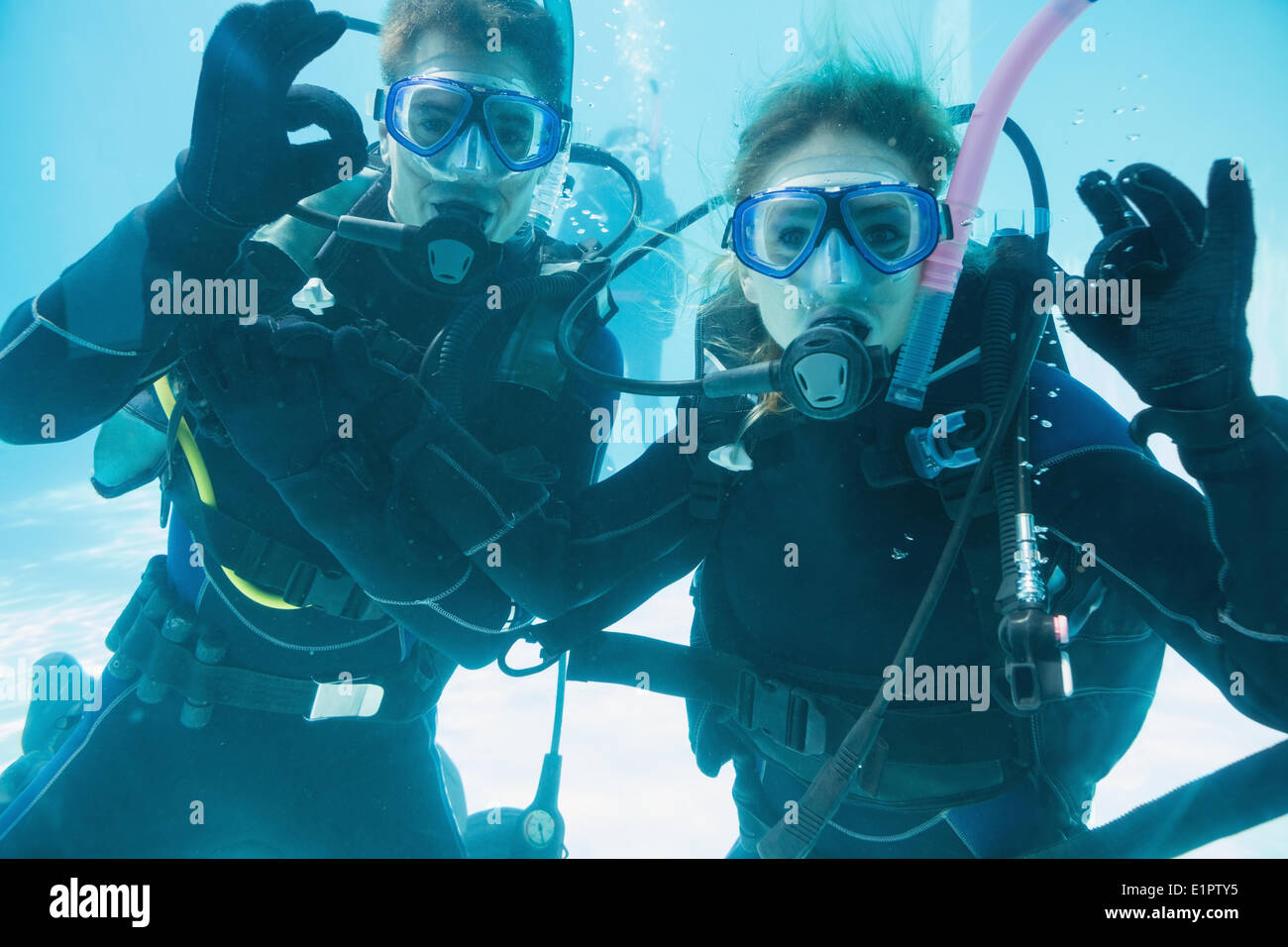 Friends on scuba training submerged in swimming pool looking to camera ...