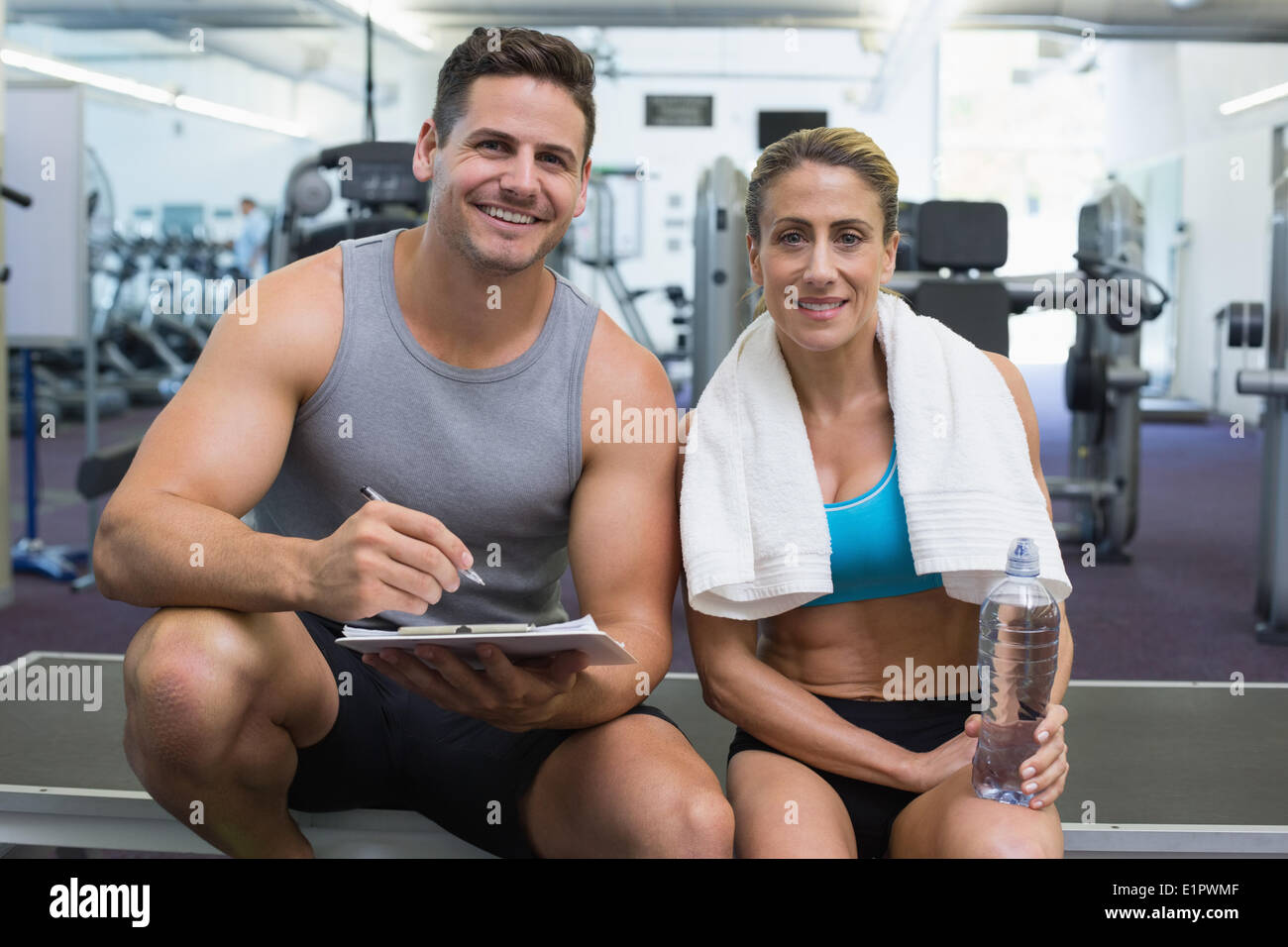 Female bodybuilder sitting with personal trainer smiling at camera ...