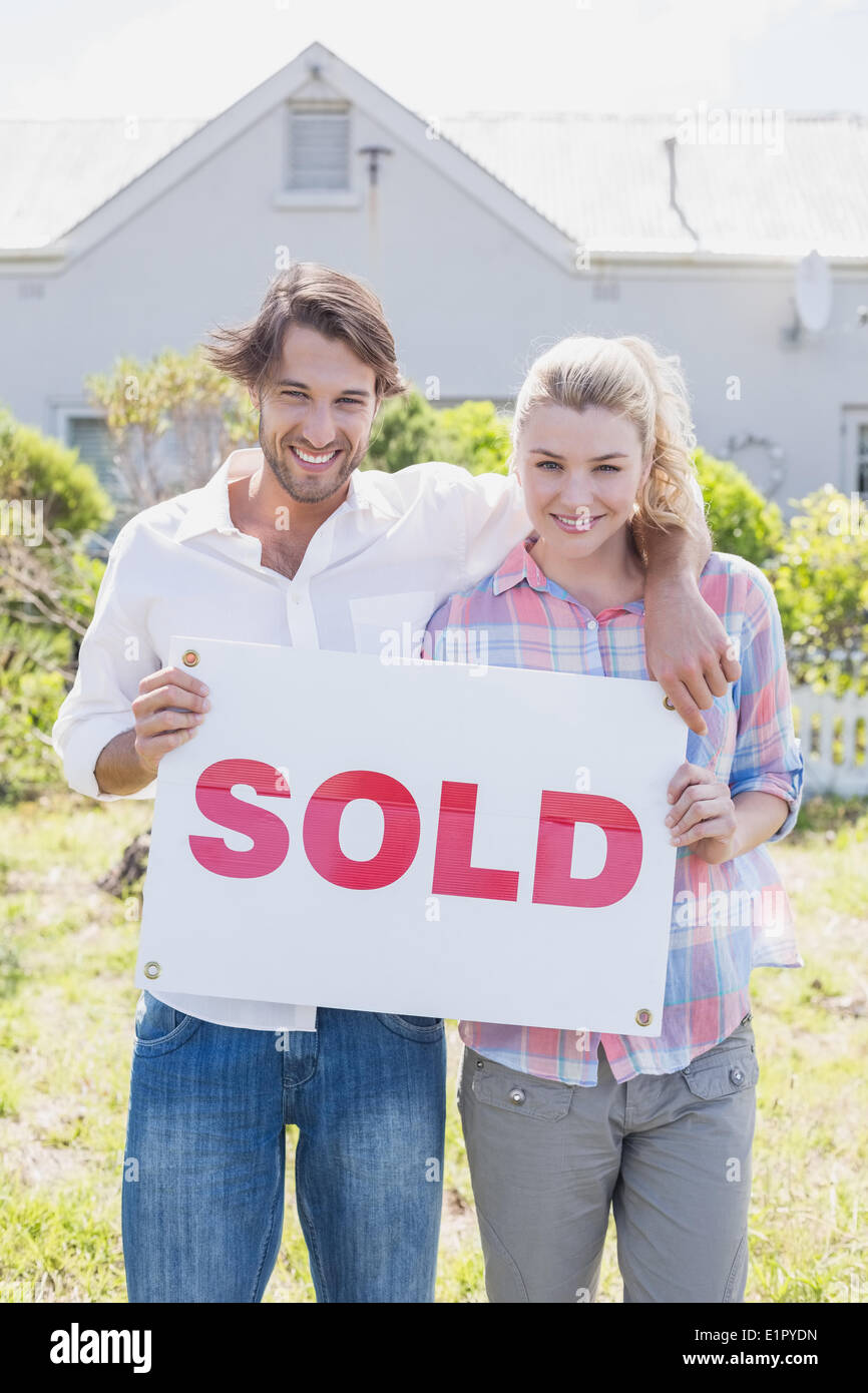 Happy couple smiling at camera holding sold sign Stock Photo - Alamy