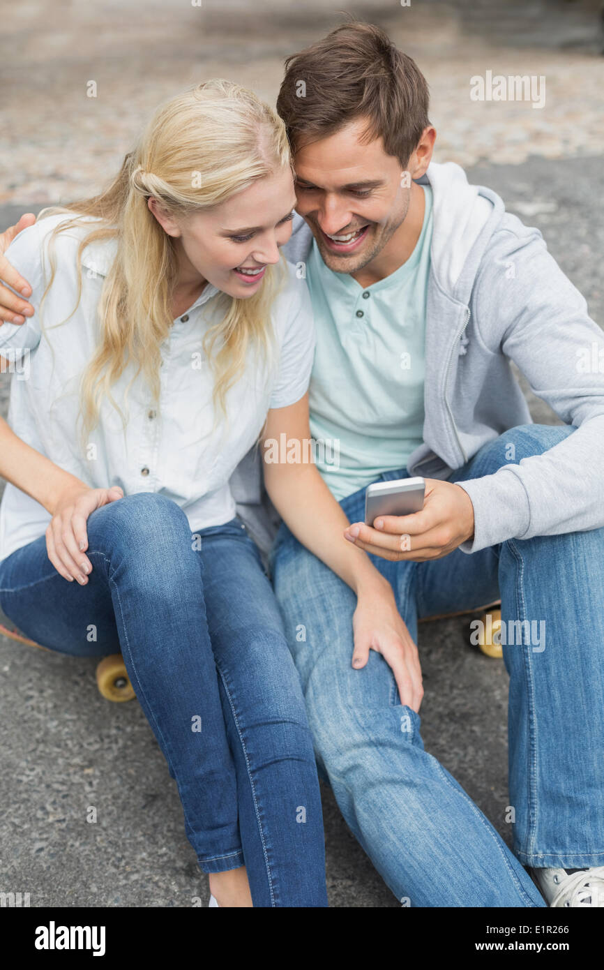 Hip young couple looking at smartphone sitting on skateboard Stock ...