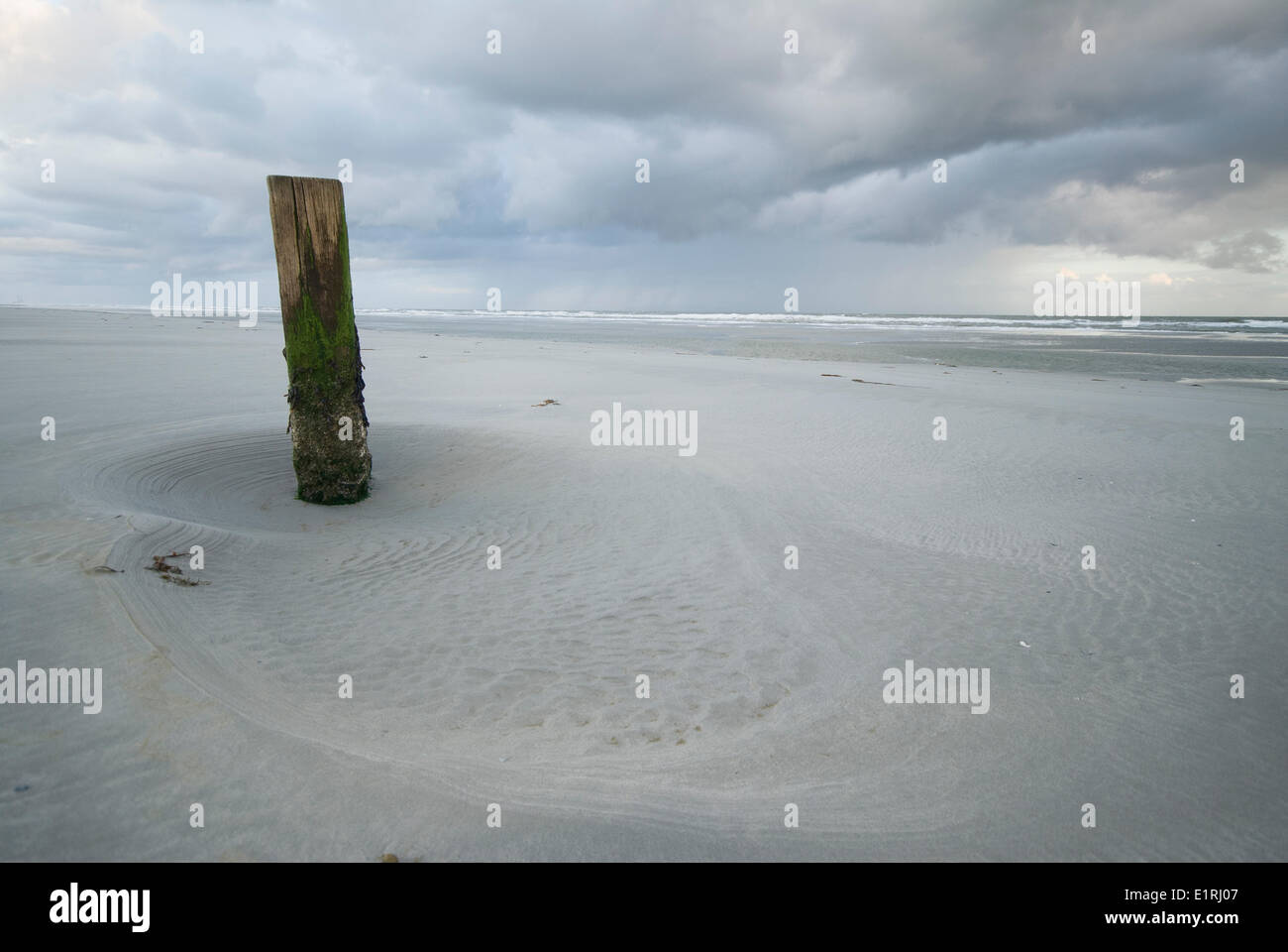 Pole on the beach at sea with dark clouds. The wind has blown a pit in ...
