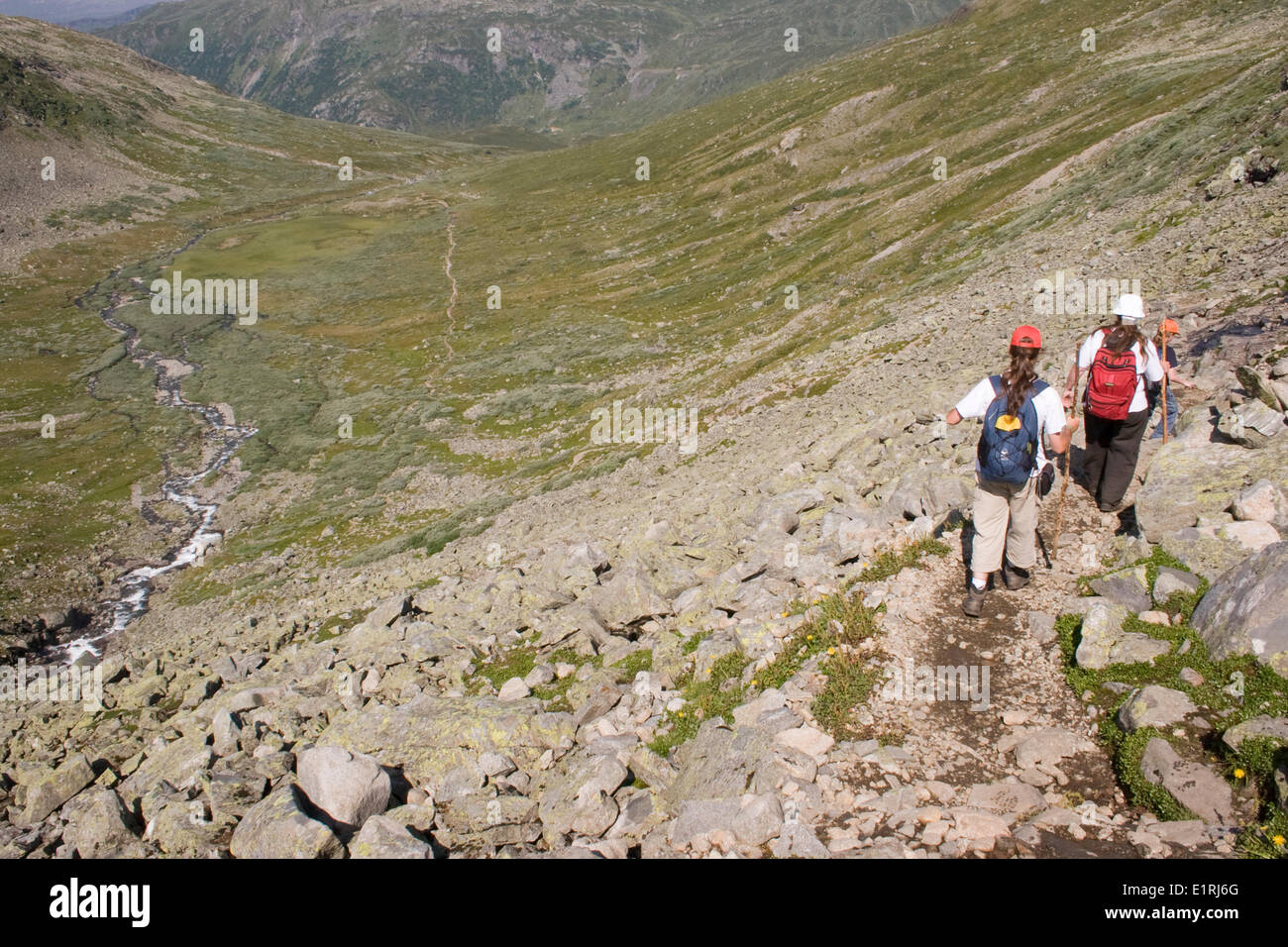 Walking family on a narrow path high above a stream in a valley in ...