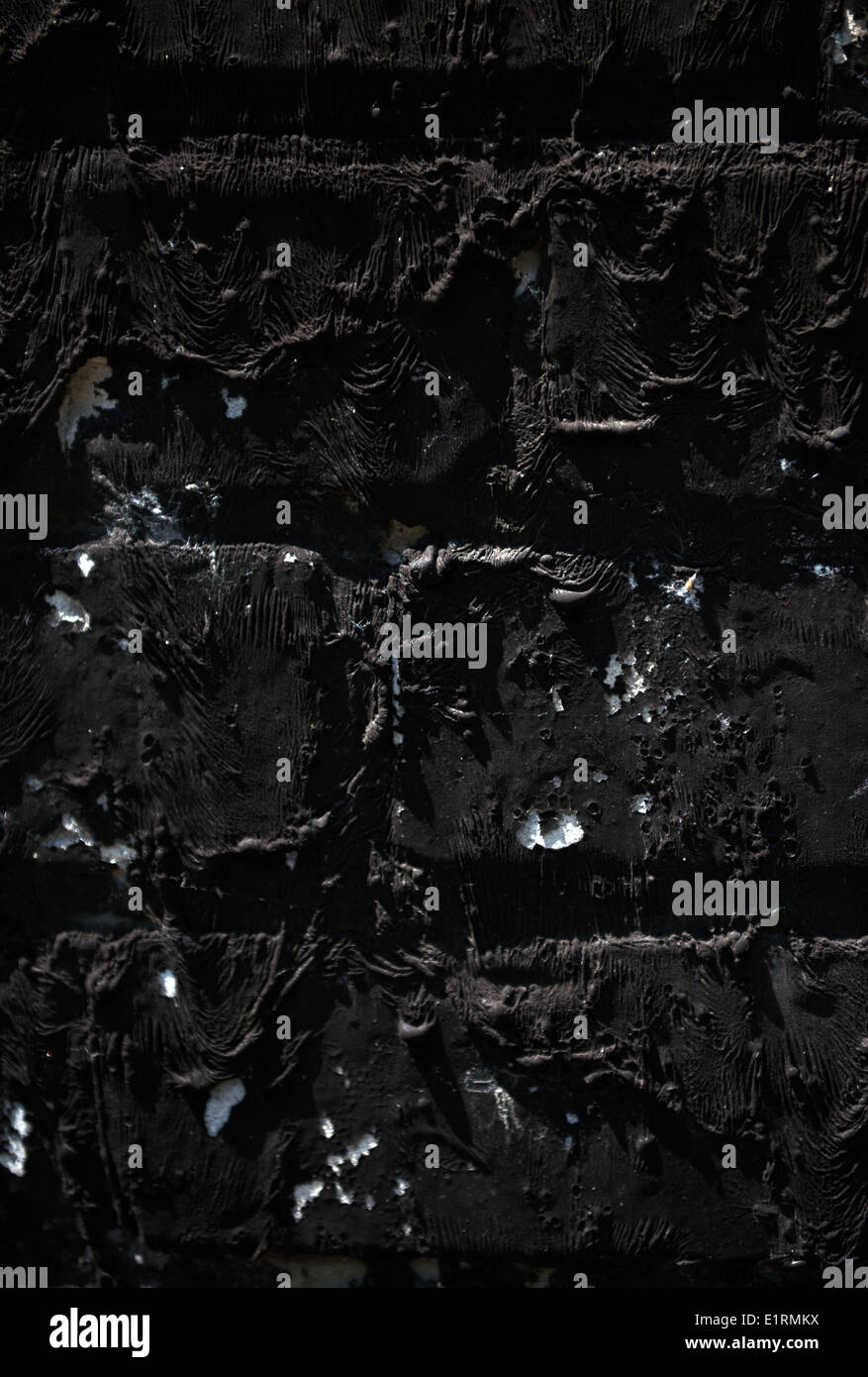 A white brick wall covered by layer and runs of black bitumen as a ...