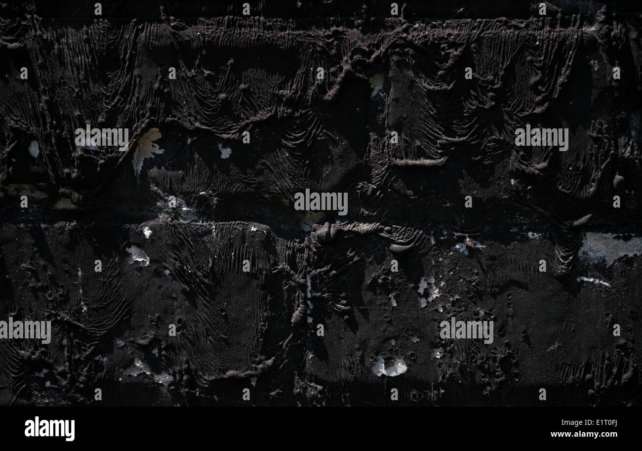 A white brick wall covered by layer and runs of black bitumen as a ...