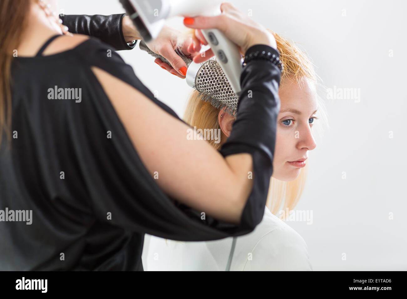 Hairdresser/Hairstyle artist working on a young woman's hair, giving it ...