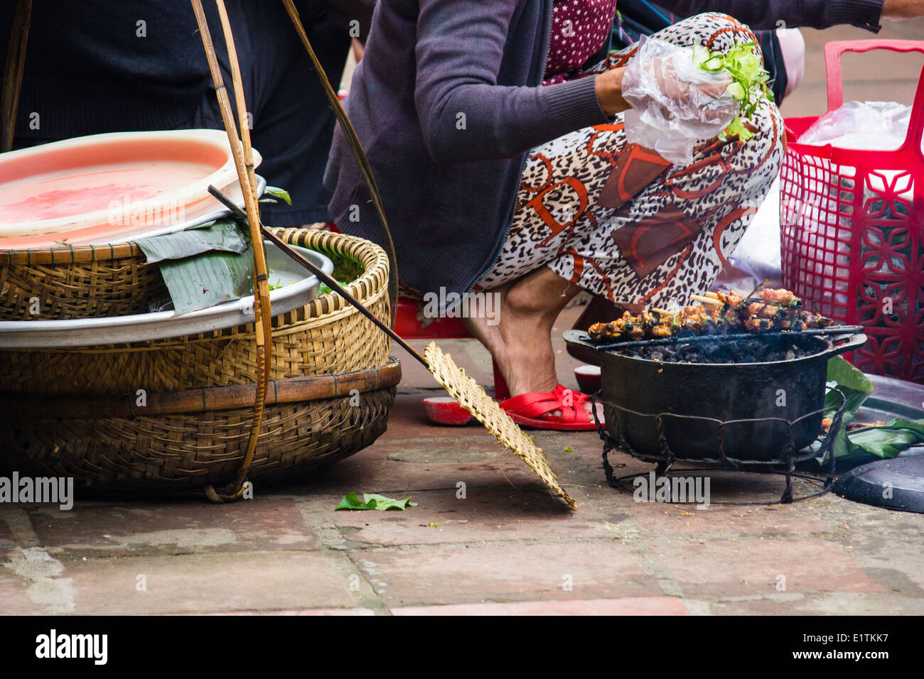 A lady cooks chicken on wooden skewers in the street of Hoi An, Vietnam ...