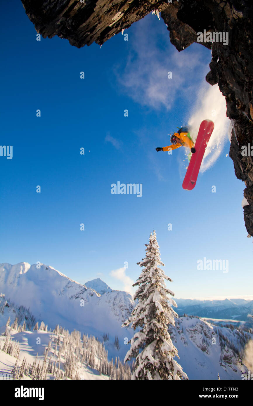 A male snowboarder catches some off a cliff on his splitboard in the ...