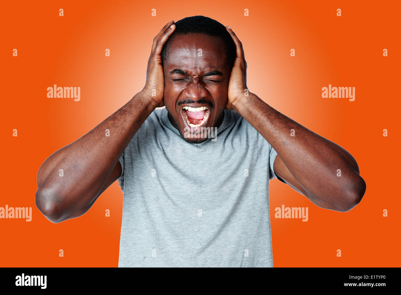 Portrait of african man shouting and closing ear by his hands on orange ...